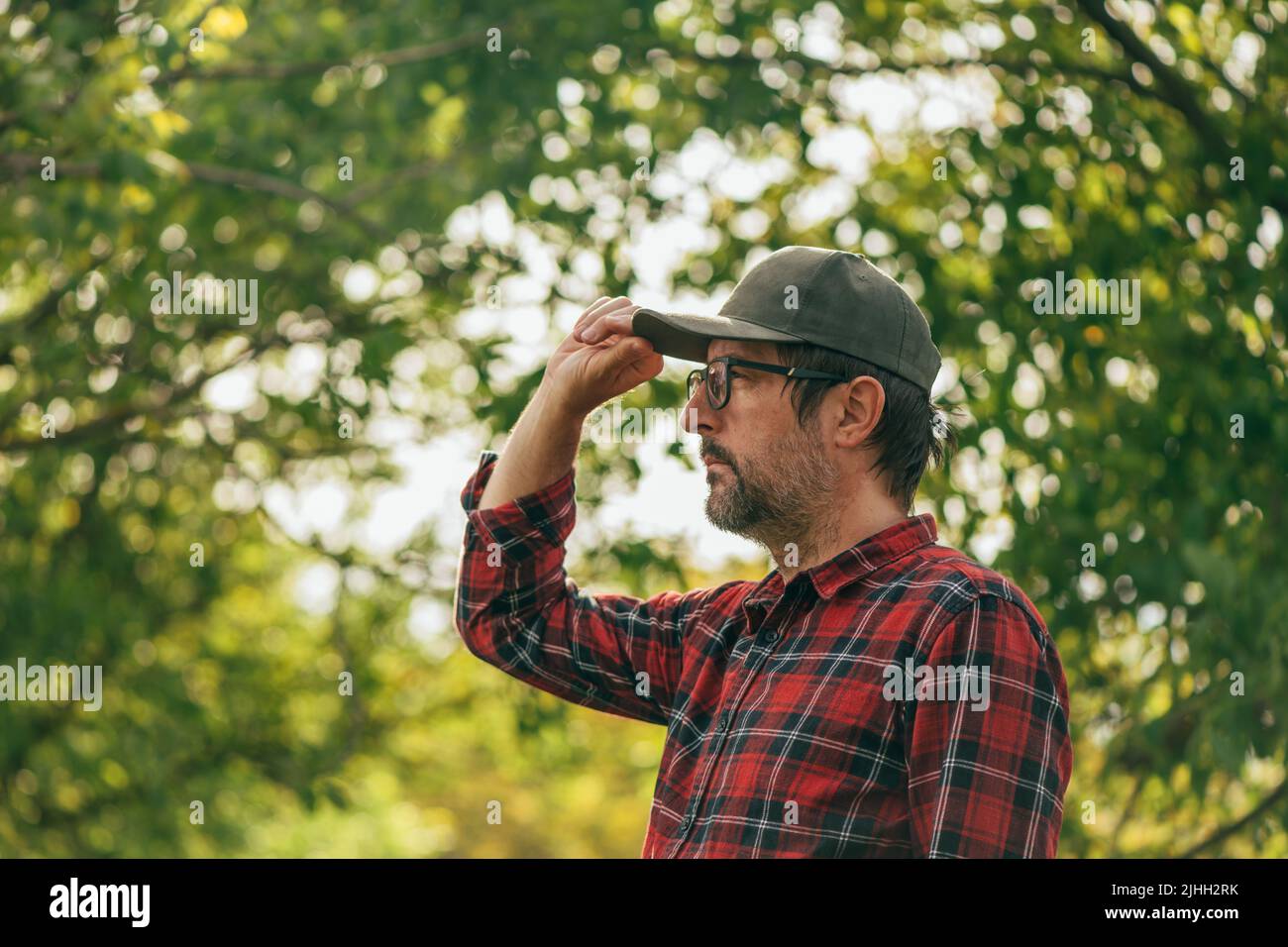 Portrait of male farmer wearing plaid shirt and trucker's hat in walnut ...