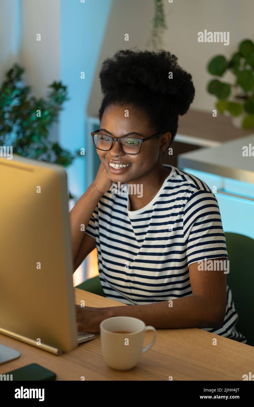 Happy African female, successful freelancer working on desktop computer ...