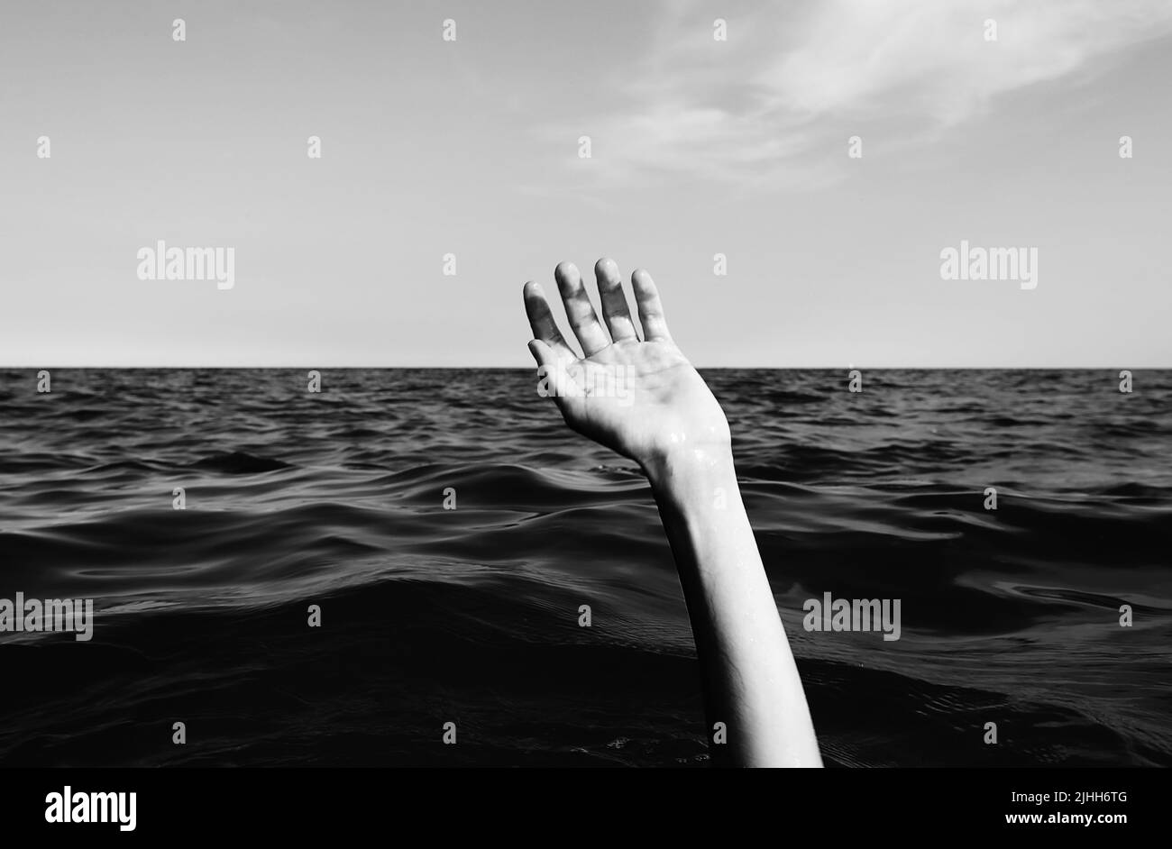 dramatic scene with the hand of the person about to drown in the sea with a black and white ...
