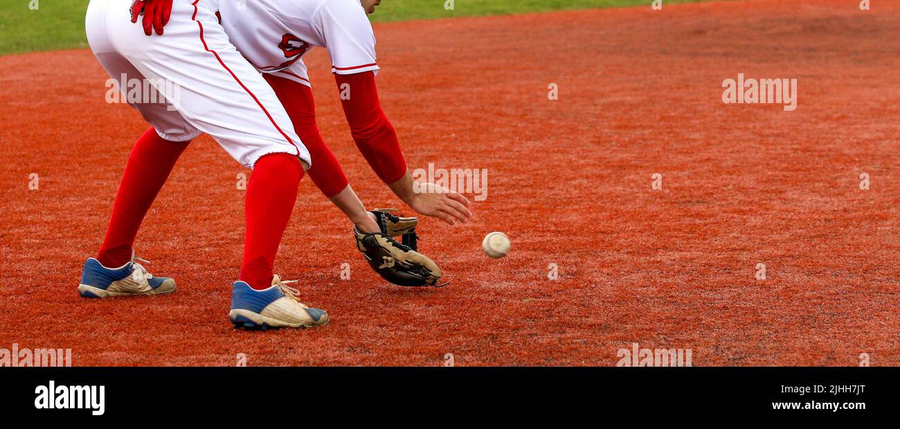 A high school baseball player fielding the ball on red turf field ...