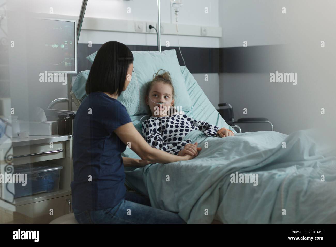 Mother sitting beside hospitalized sick daughter resting in hospital ...