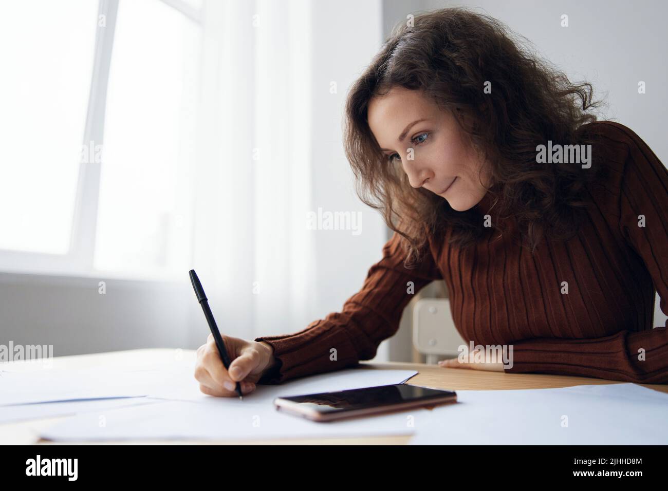 Wide angle shot of pensive serious focused curly woman writing script ...