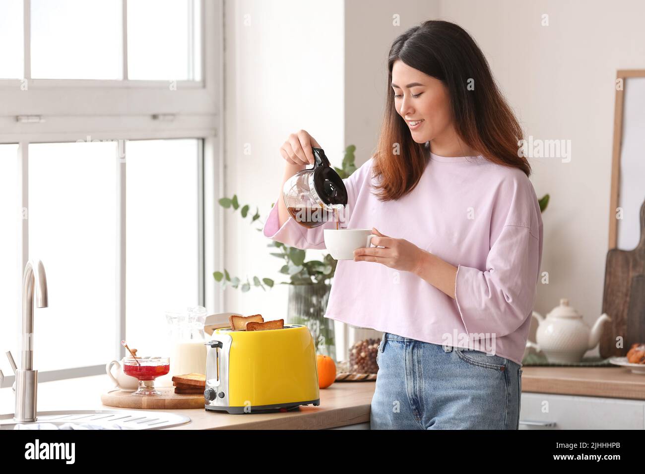 Beautiful young Asian woman drinking coffee and making tasty toasts in ...