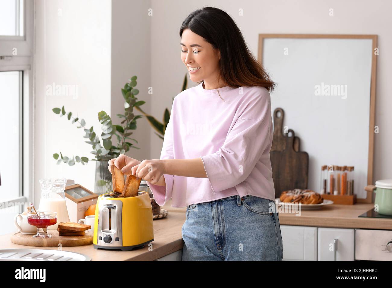 Beautiful young Asian woman making tasty toasts in kitchen Stock Photo ...
