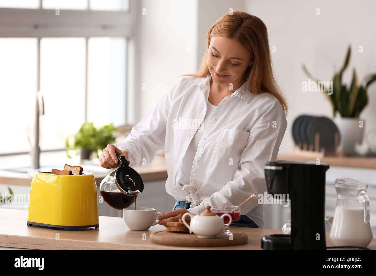 Mature woman making tasty toasts and drinking coffee in kitchen Stock ...