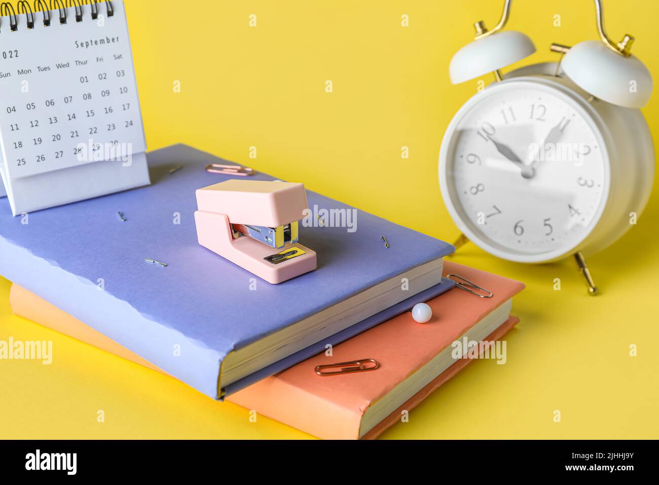 Stapler with books, alarm clock and calendar on yellow background ...