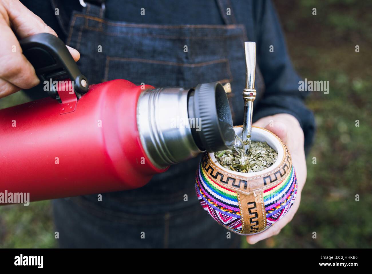 unrecognizable woman serving mate with a red thermo, in a colorful ...