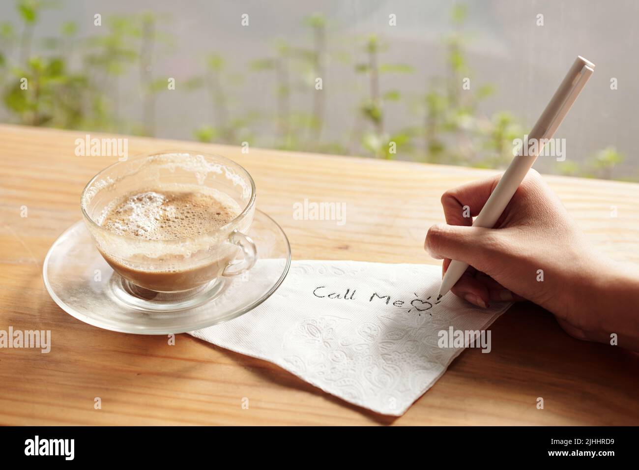 Young woman drinking cup of coffee, writing call me on napkin and ...