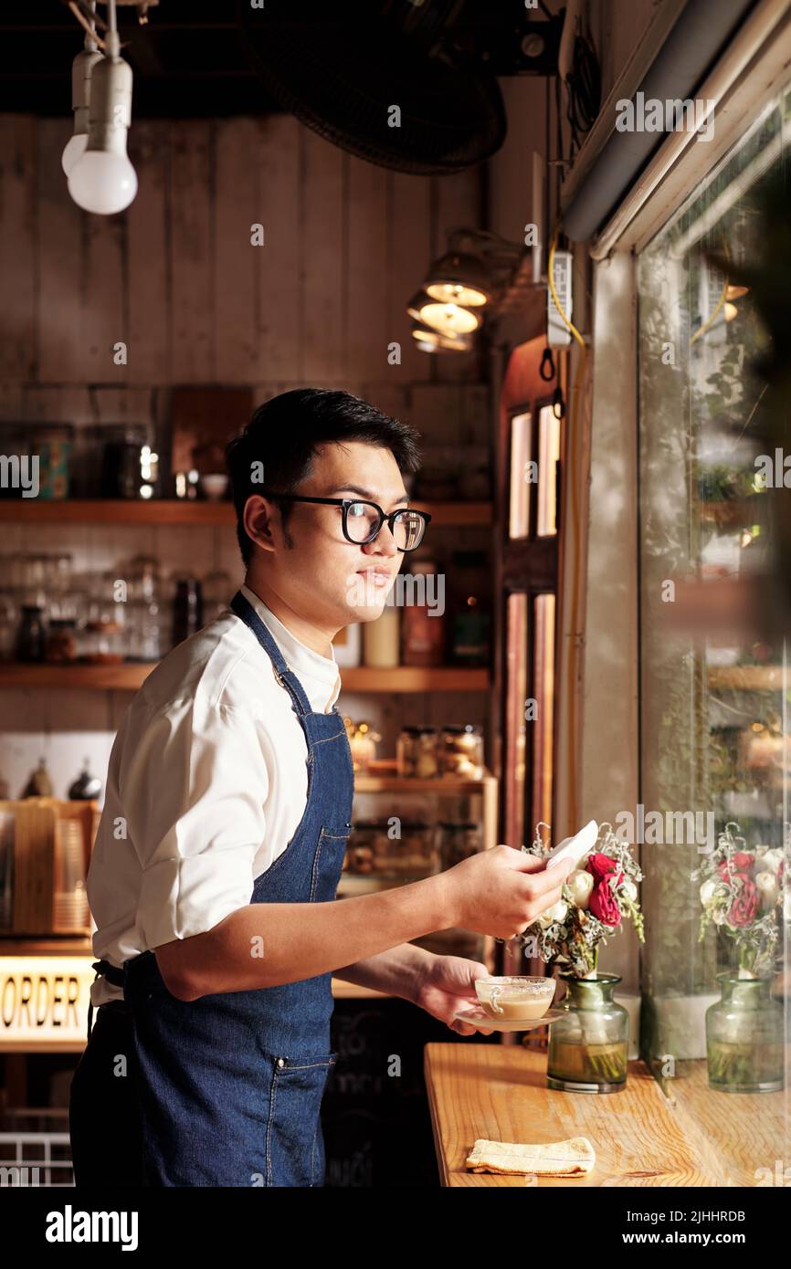 Surprised young barista looking through window after reading love note ...