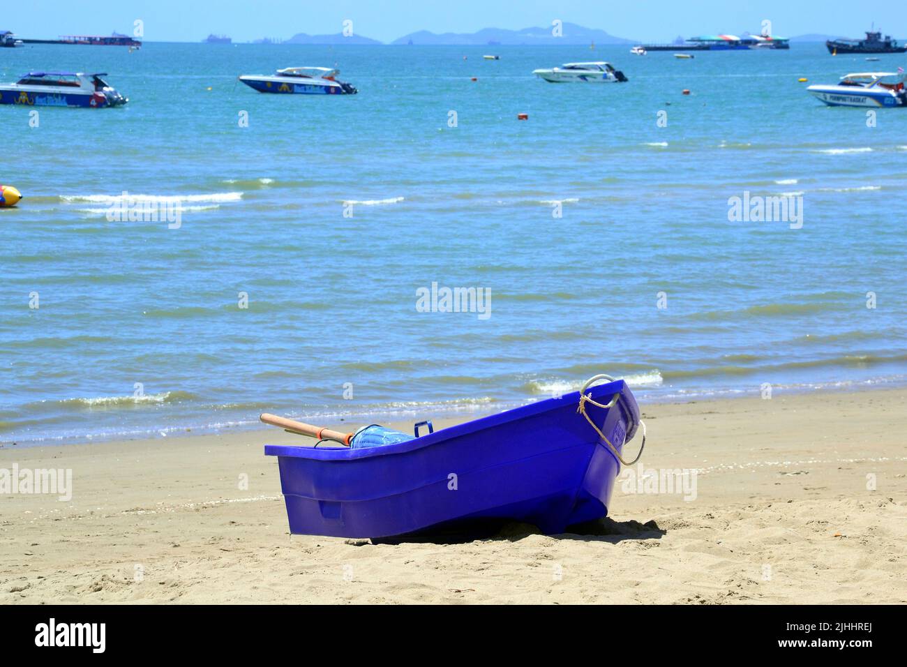 A small, empty, blue plastic rowing boat sits on the sandy beach at the ...