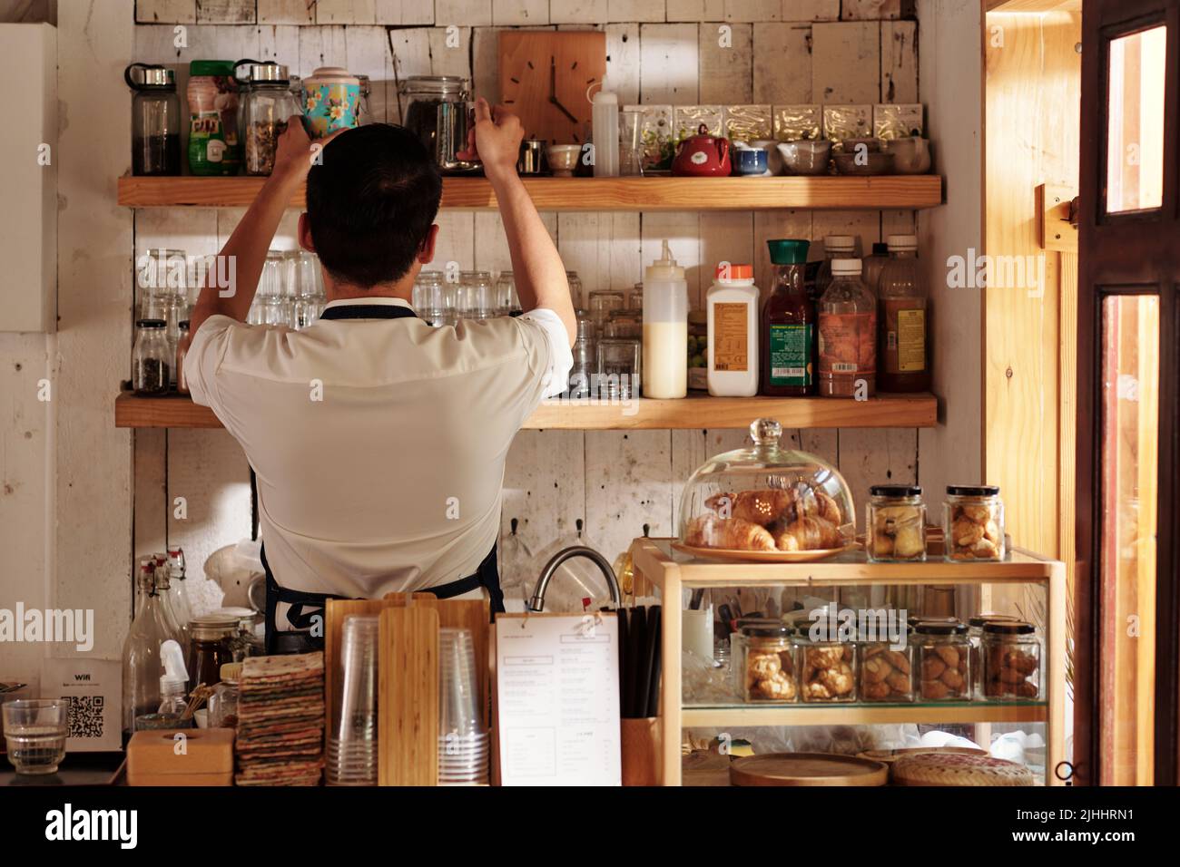 Coffeeshop barista taking jars with black tea from shelf to make drink ...