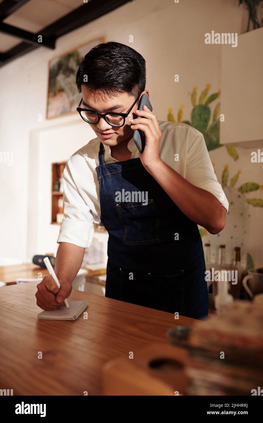 Cafe waiter talking on phone with customer and writing down order ...