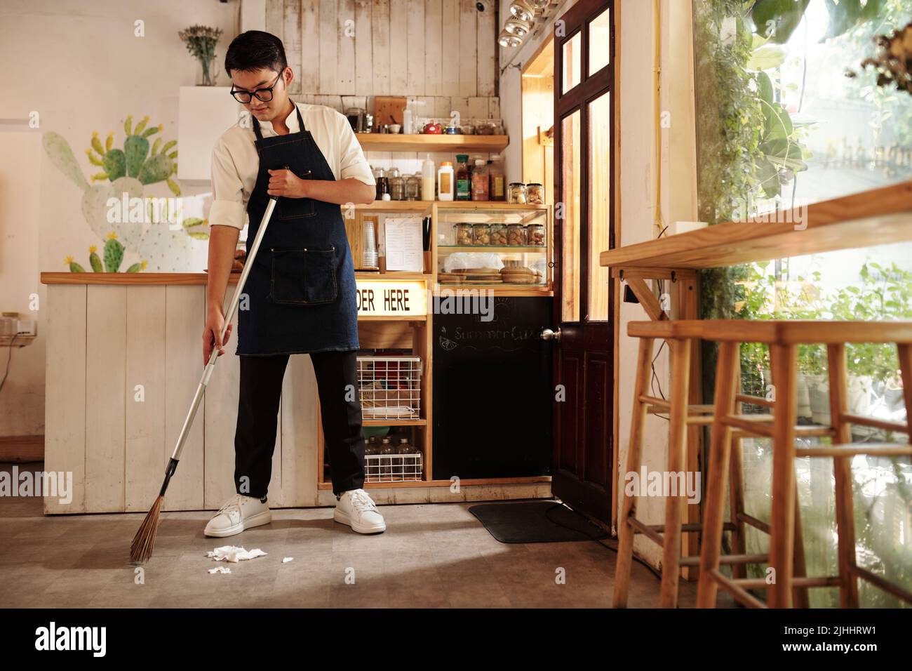 Small business owner sweeping floor in his coffeeshop after closing ...