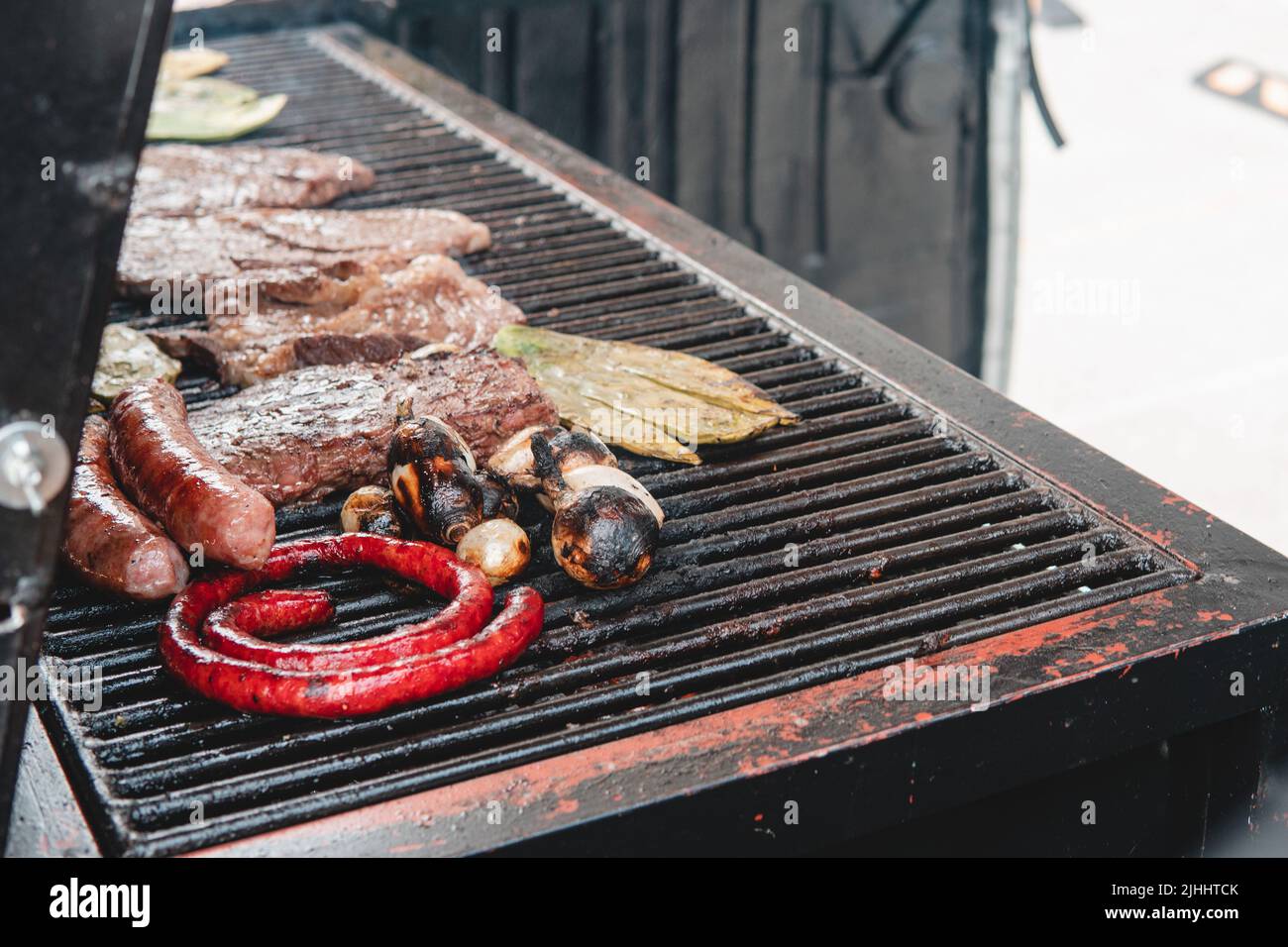 Side view of a grill full of cuts of meat vegetables and sausages. High ...