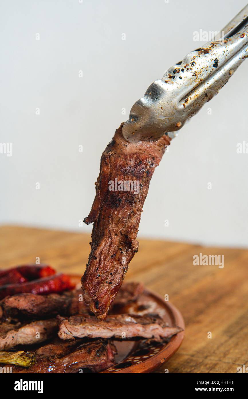 Cut of meat with a tong. The person serving meat in a clay dish. High ...