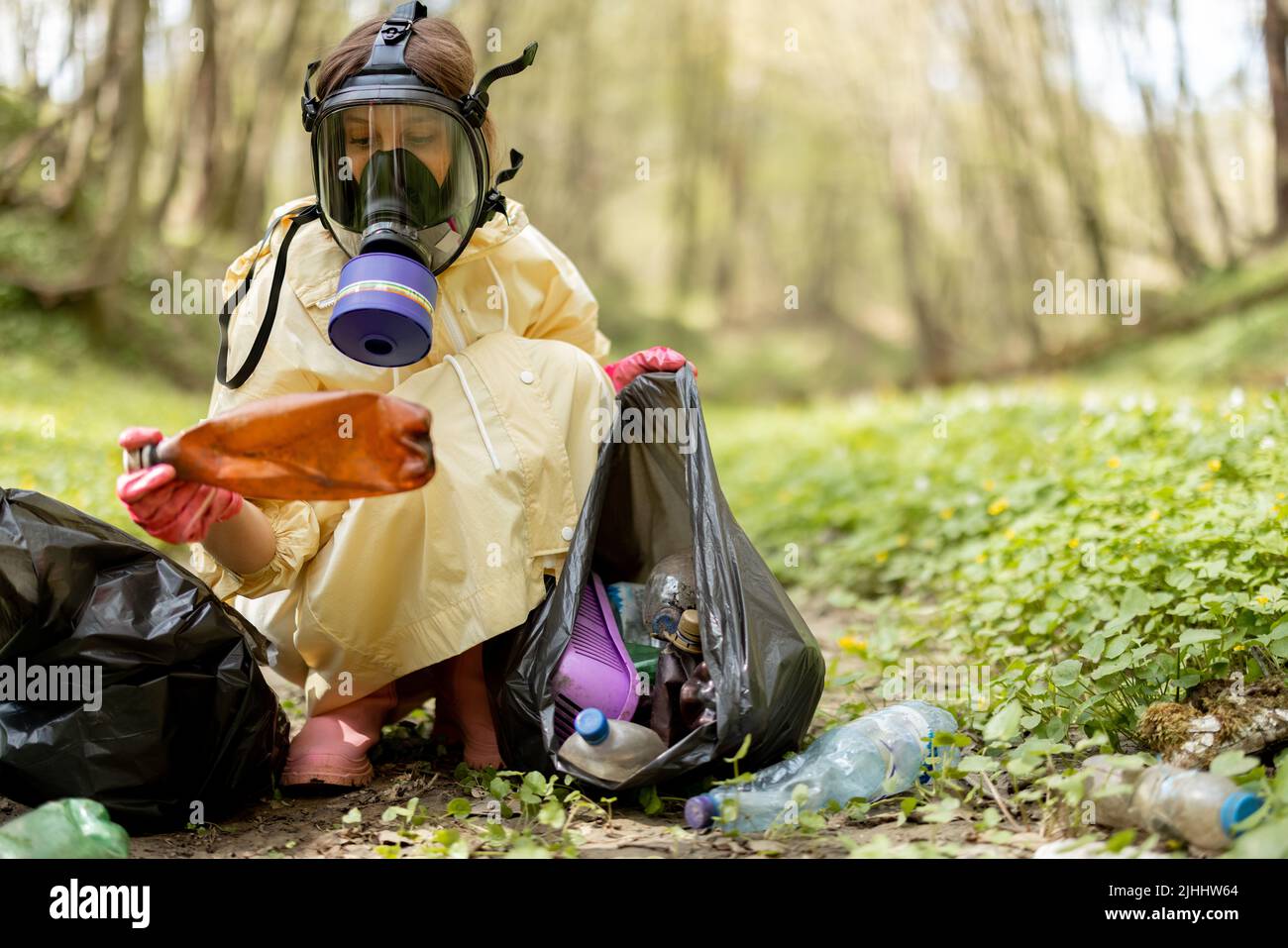 Woman in gas mask and protective clothes collecting scattered plastic ...