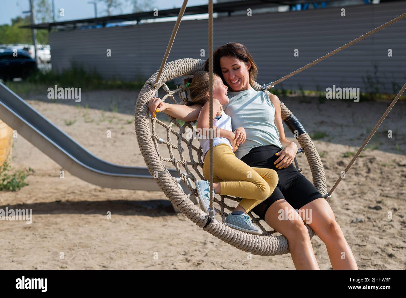 Mom and daughter swing on a round swing. Caucasian woman and little girl have fun on the ...