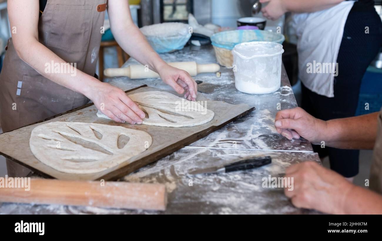 A baker shapes and cuts traditional French Fougasse bread. Front view ...