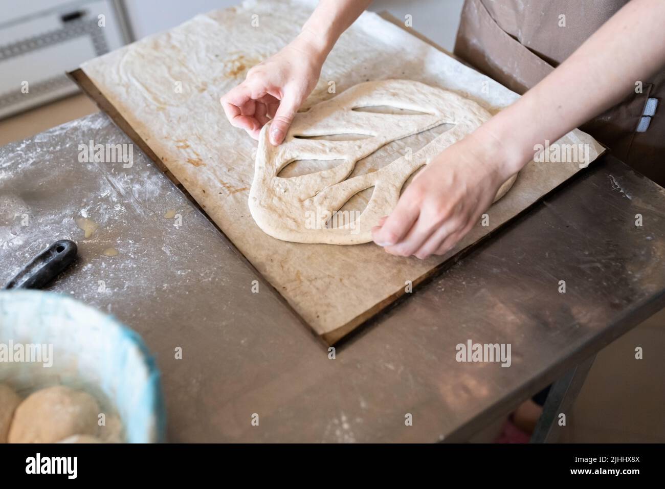 A baker shapes and cuts traditional French Fougasse bread. Front view ...
