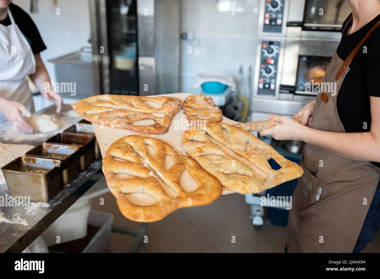 A woman in a bakery takes traditional French Fougasse bread out of the ...