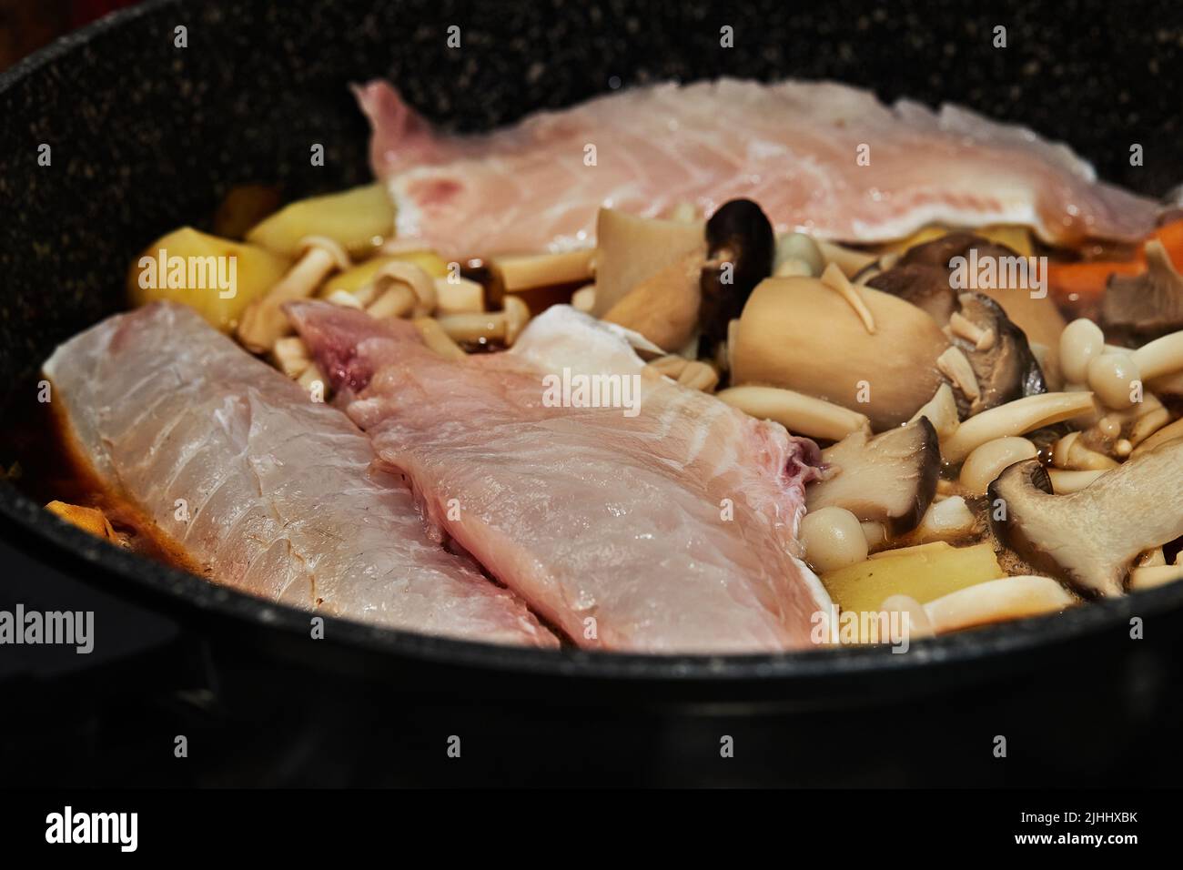 Fish stewed with carrots, mushrooms and potatoes is fried in pan on gas ...