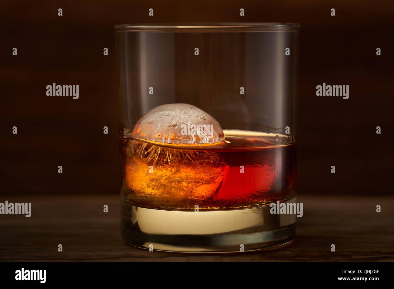 A glass of whisky with round big ice cube inside Stock Photo - Alamy