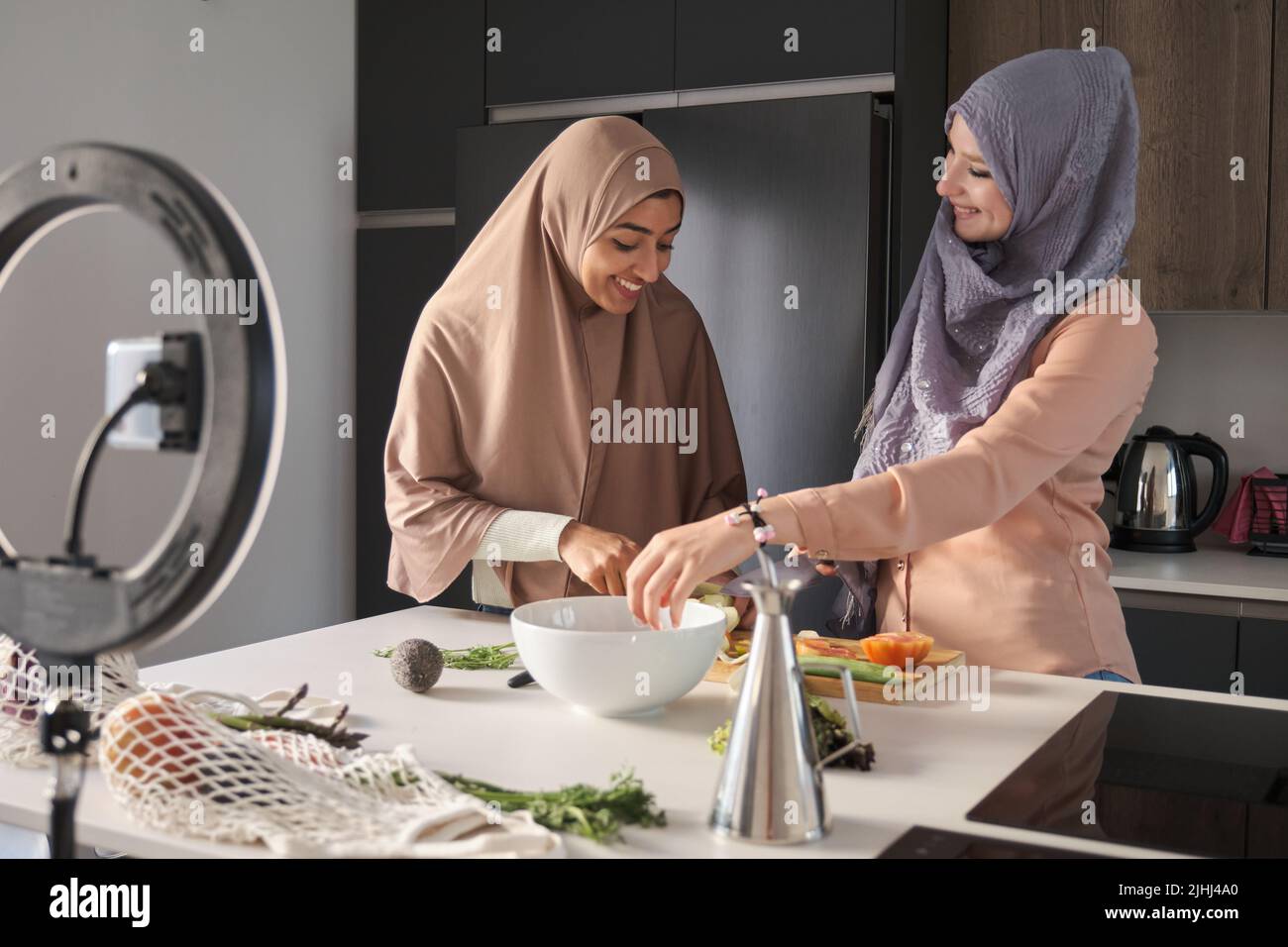 Two muslim food vloggers laughing while preparing a salad at kitchen ...