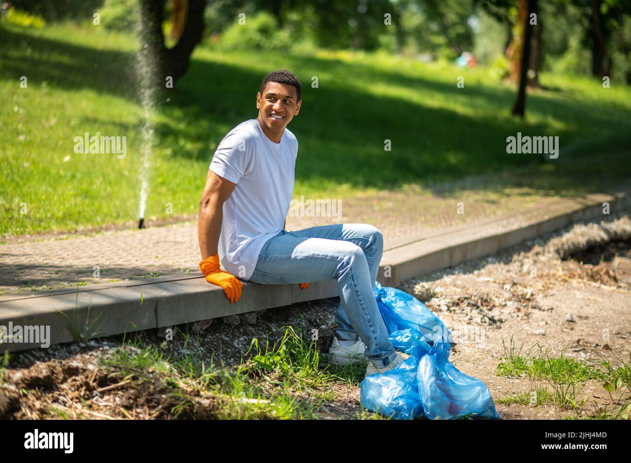 Dark-skinned man sitting in park smiling to side Stock Photo - Alamy
