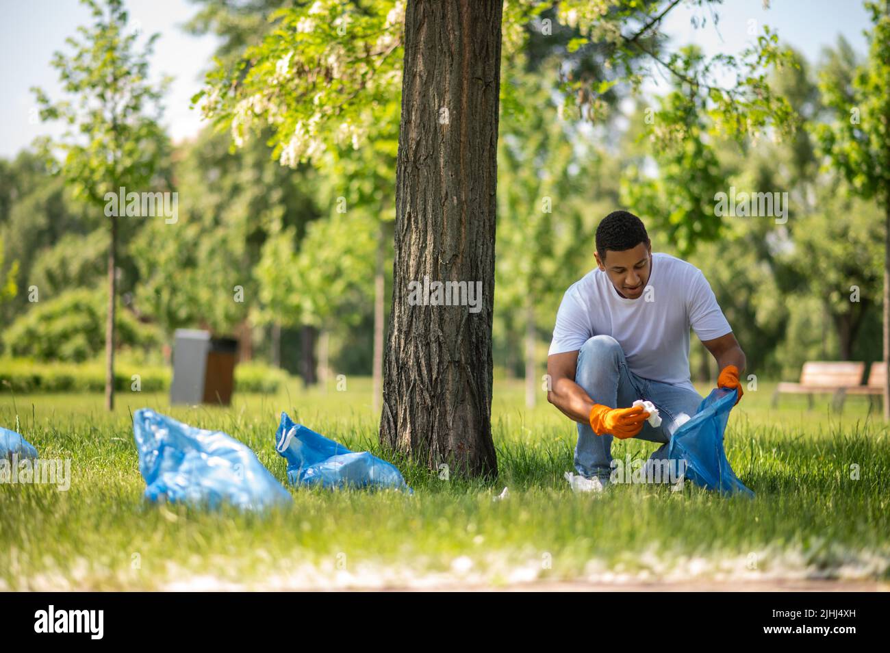 Guy crouching near tree picking up garbage Stock Photo - Alamy