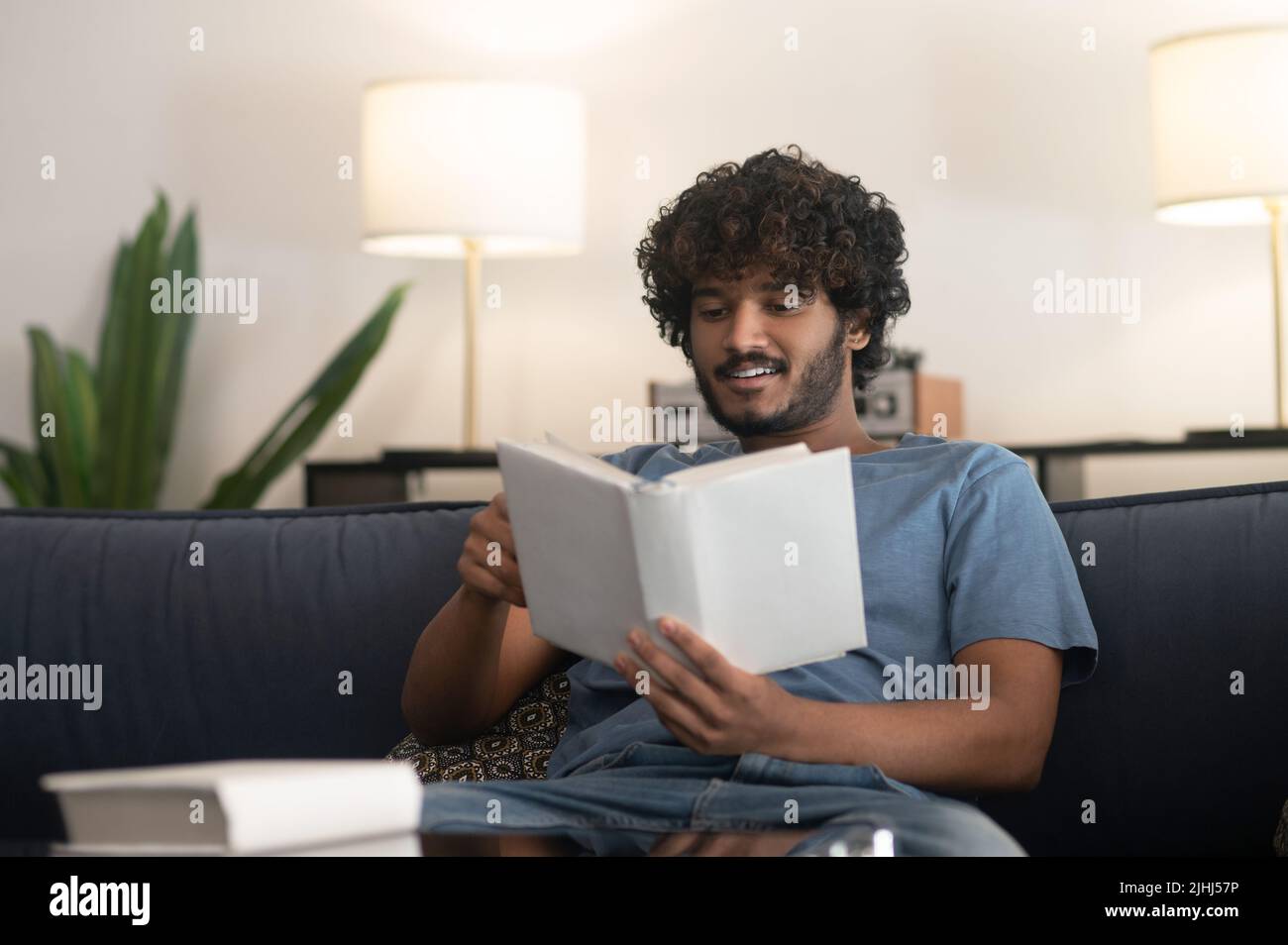 Curly-haired indian guy reading a book and looking involved Stock Photo ...