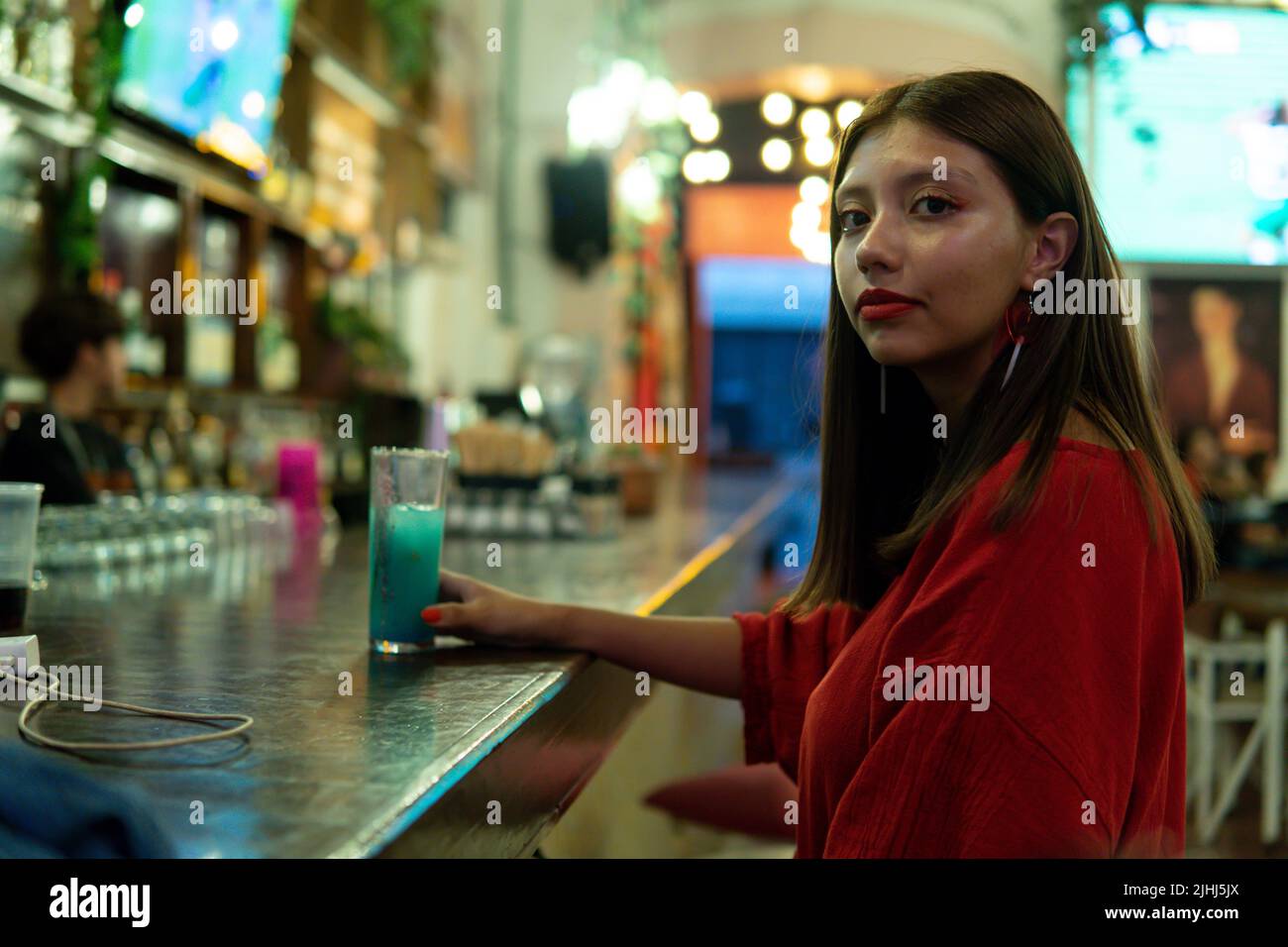 A young Latin woman enjoying a drink at a bar alone. Girl in a red ...