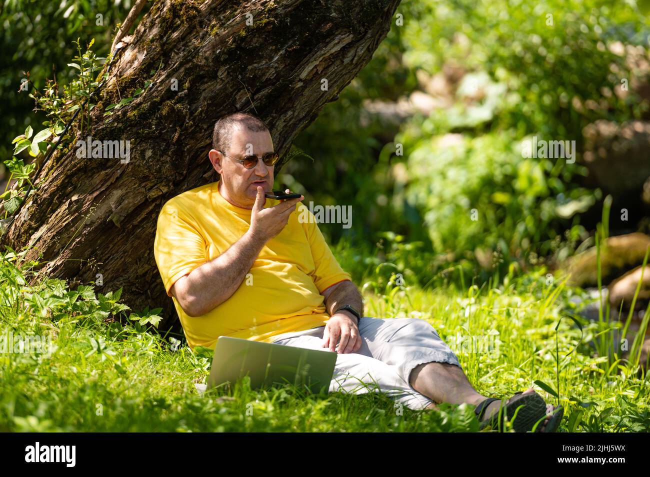 man with laptop and smartphone working outside in the meadow by the ...