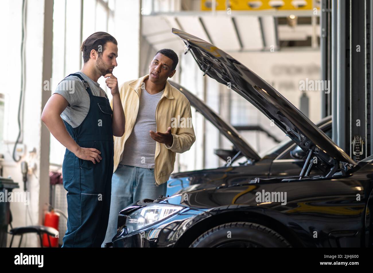 Mechanic and client standing near car hood Stock Photo - Alamy