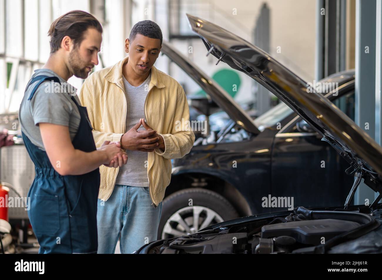 Two men talking about problem near hood of car Stock Photo - Alamy