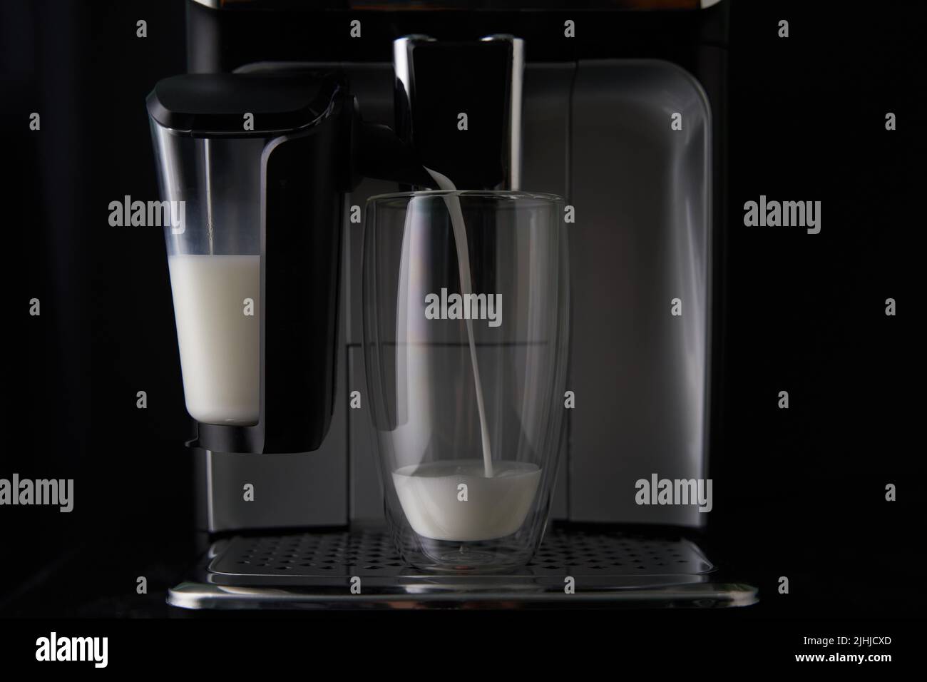 Freshly brewed latte is poured from the coffee machine into glass cups ...