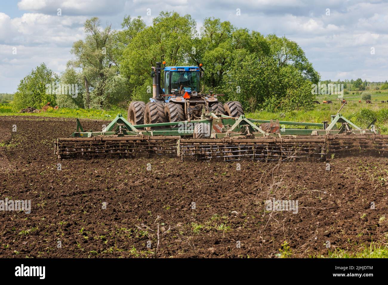 Blue tractor with double wheels pulling disc harrow with roller basket ...