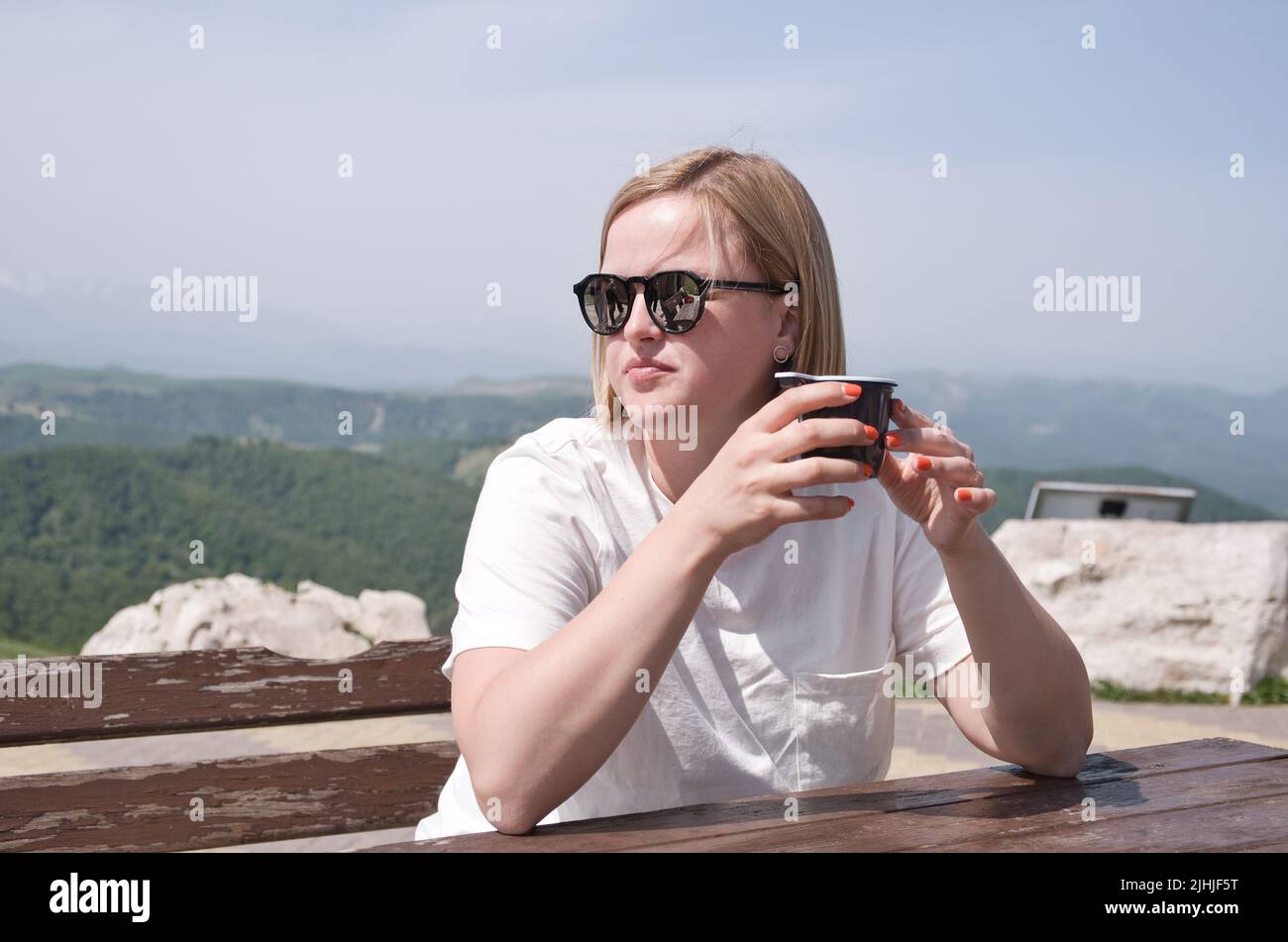 Woman in white t-shirt and black sunglasses drinking warm tea in the ...