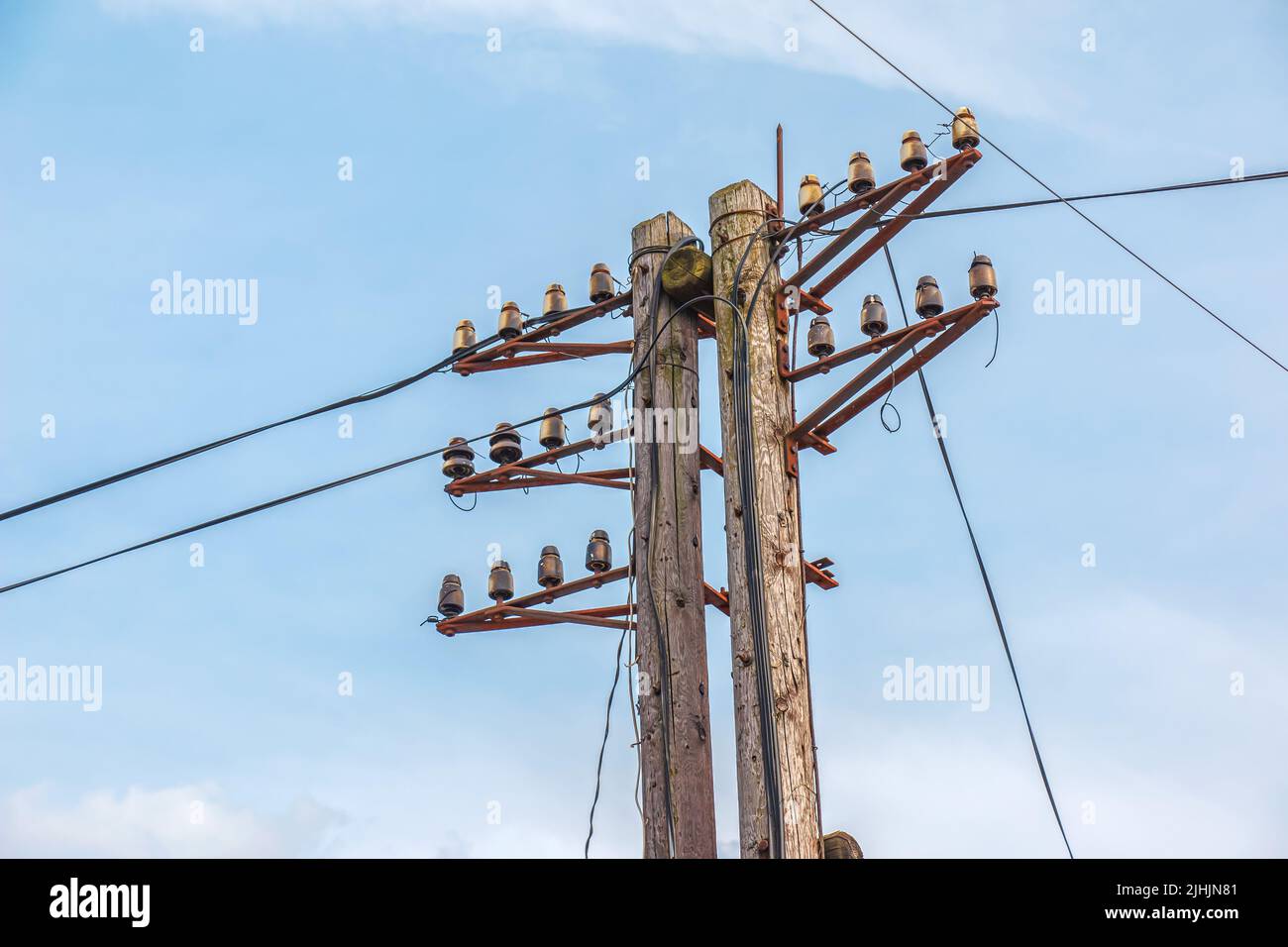 An old, rotten wooden pole with electrical insulators and cut-off wires ...