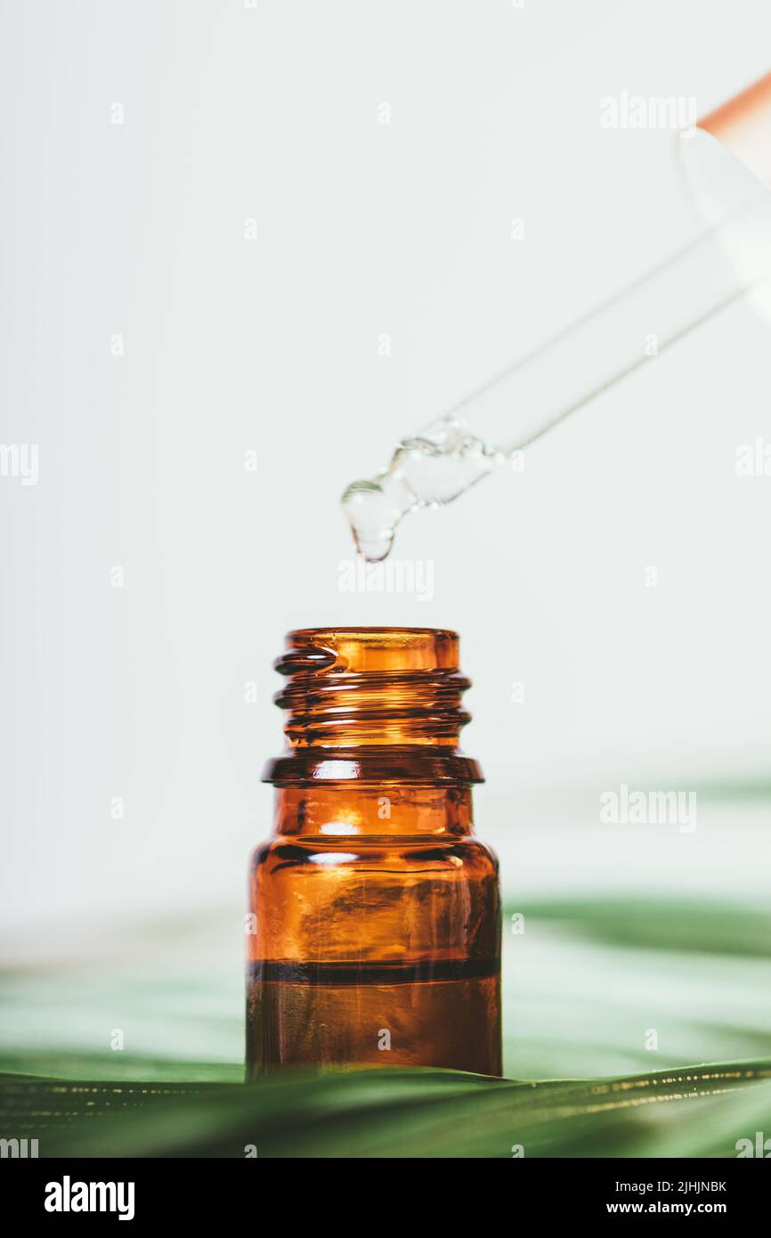 Drop of essential oil drips from pipette into bottle on white ...