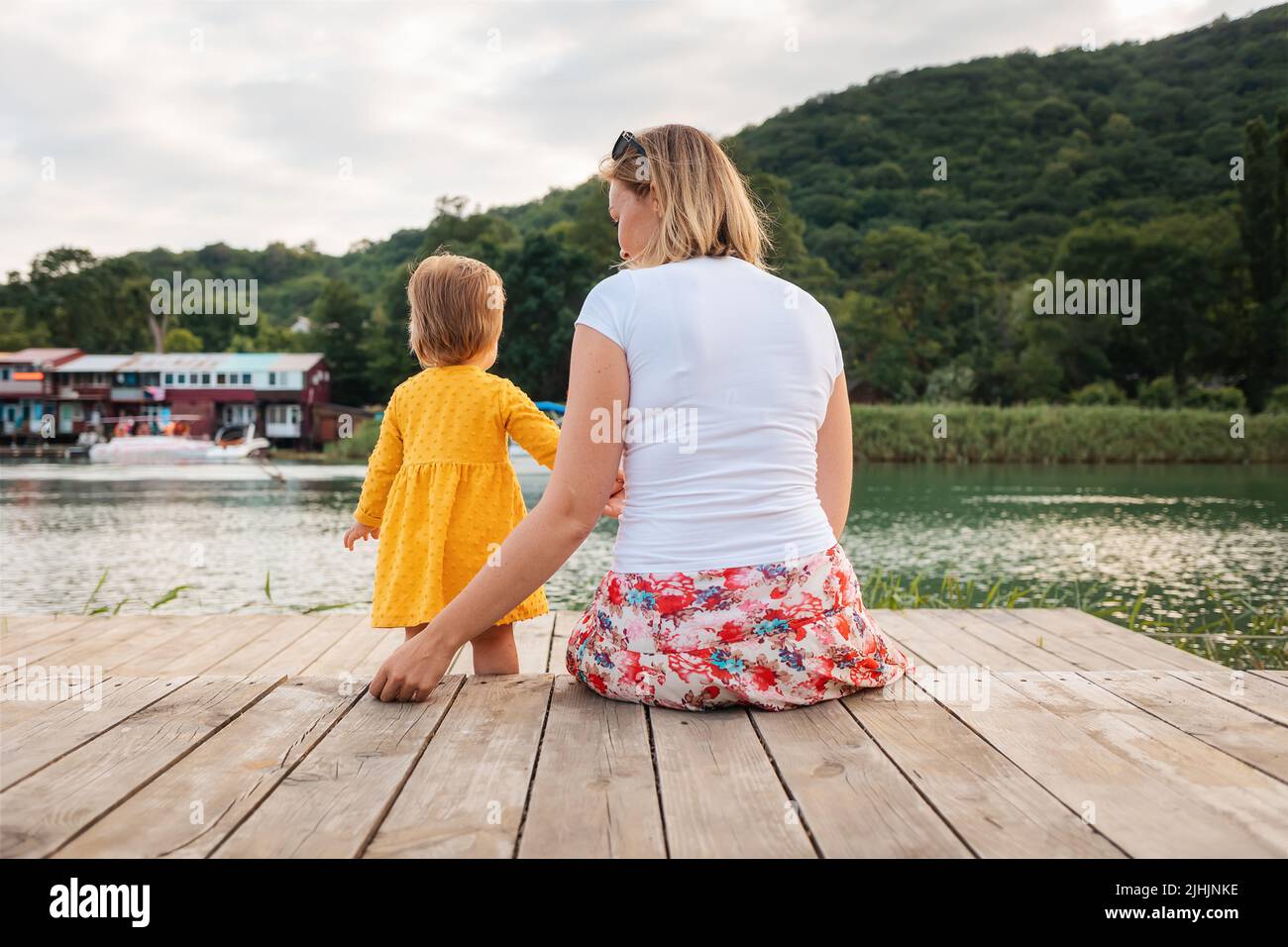 A mother and baby girl sitting on the pier. Back view. The concept of ...