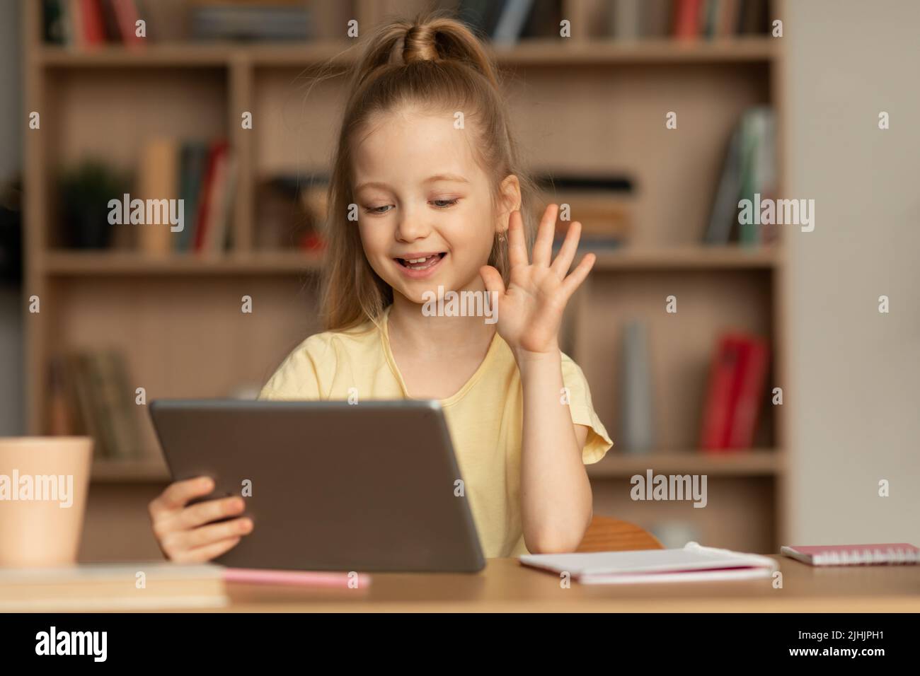 Schoolgirl Waving Hello To Digital Tablet Making Video Call Indoors ...