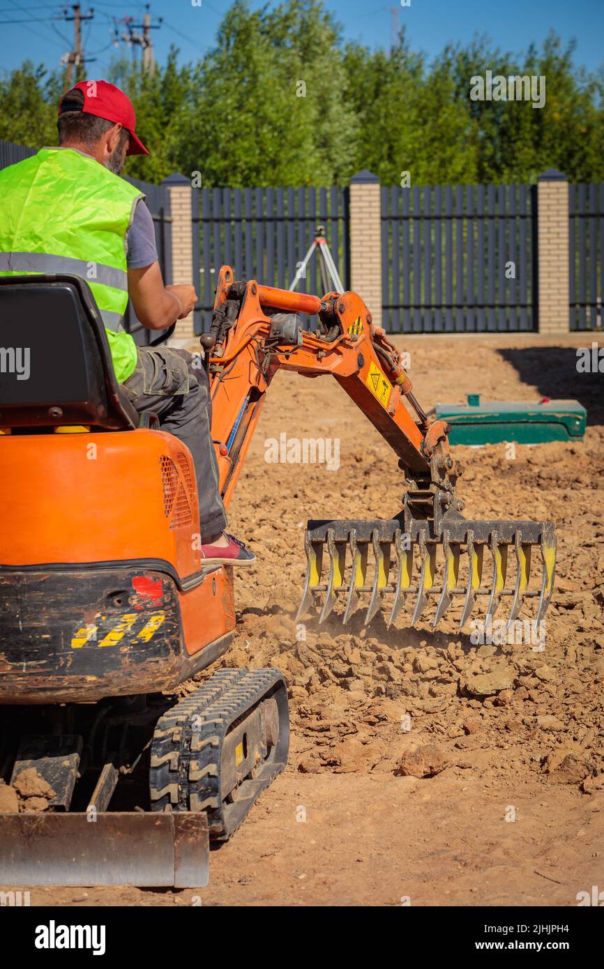 A man on a mini-excavator levels a piece of land, loosens the soil ...