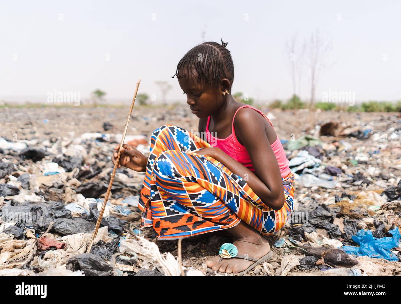 Young African girl listlessly poking through a pile of rubbish, forced ...
