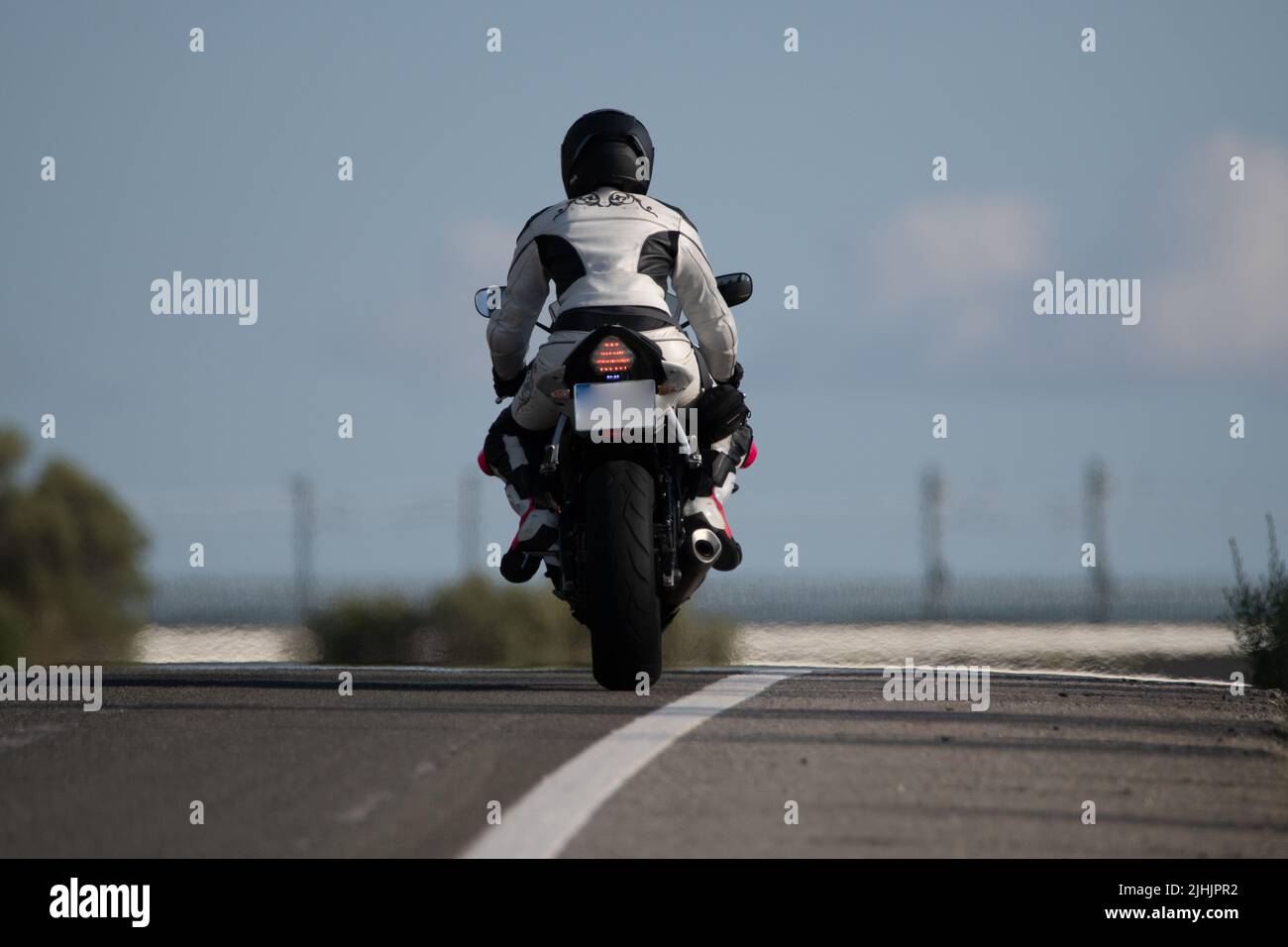 back view of a young biker woman dressed in a leather protection suit ...
