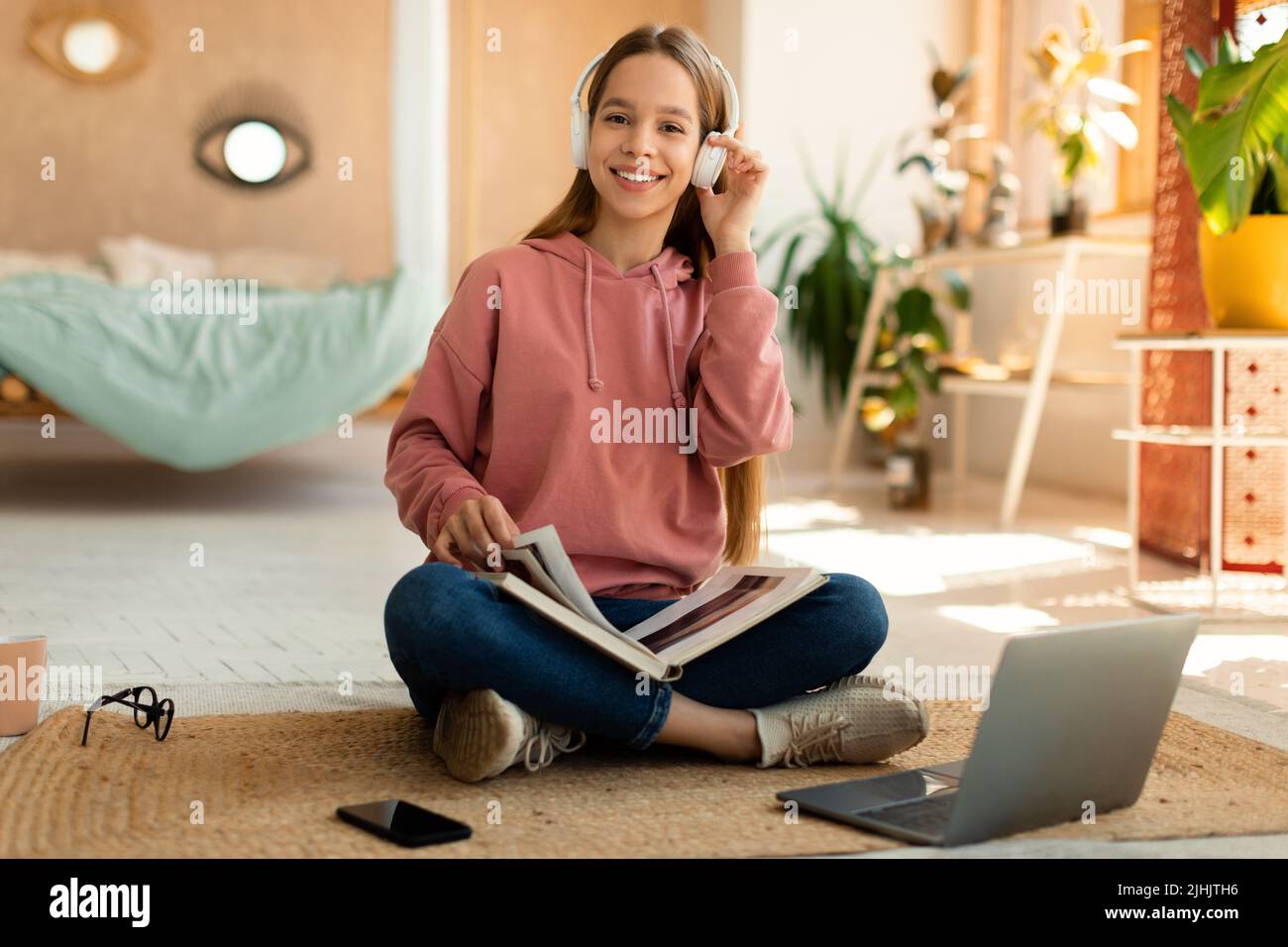 Happy teenage female student in headphones reading book during online ...
