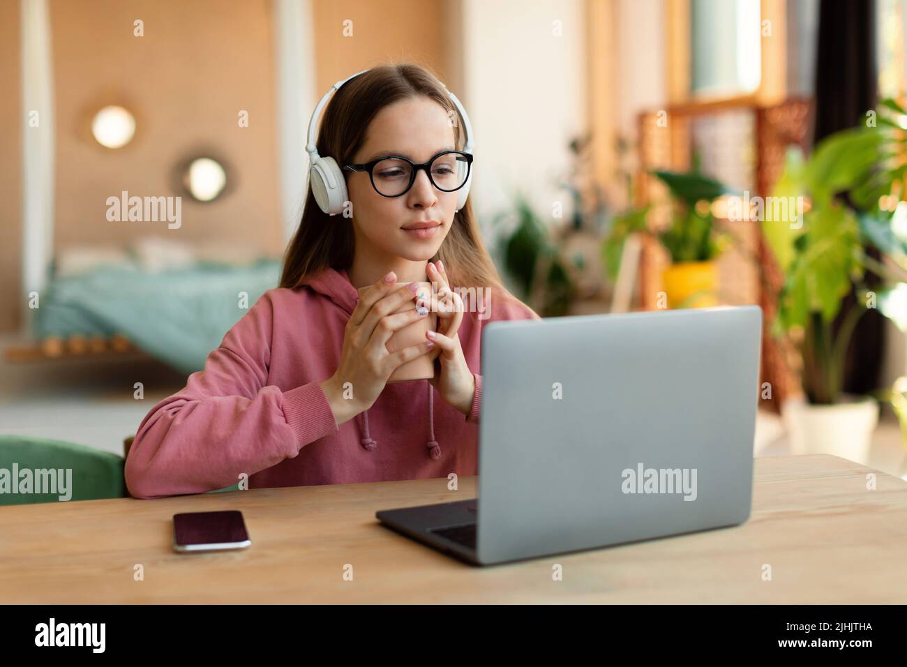 Concentrated teen girl watching online lesson on laptop and drinking ...