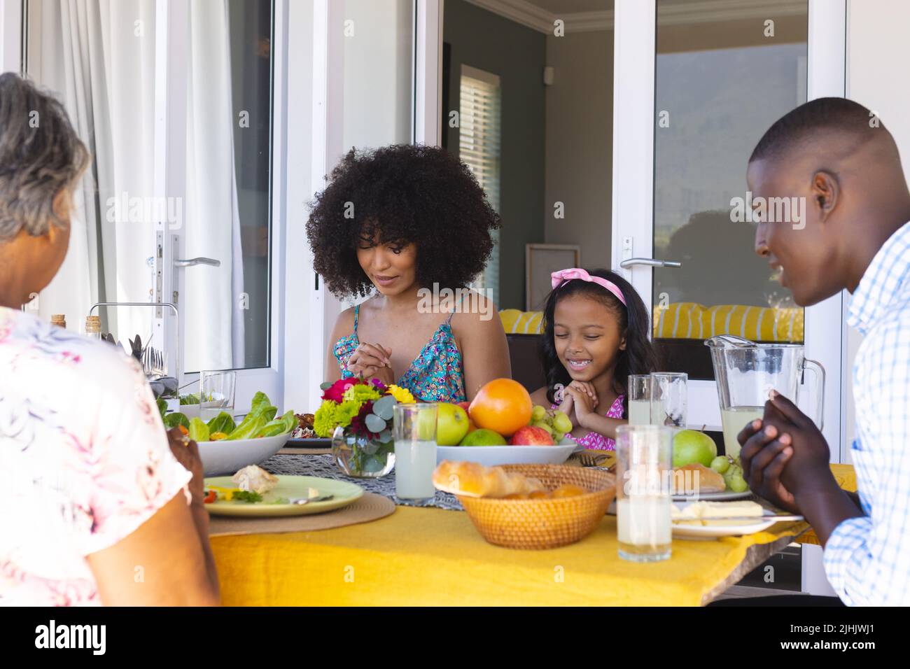 Multiracial multigeneration family praying before having lunch while ...