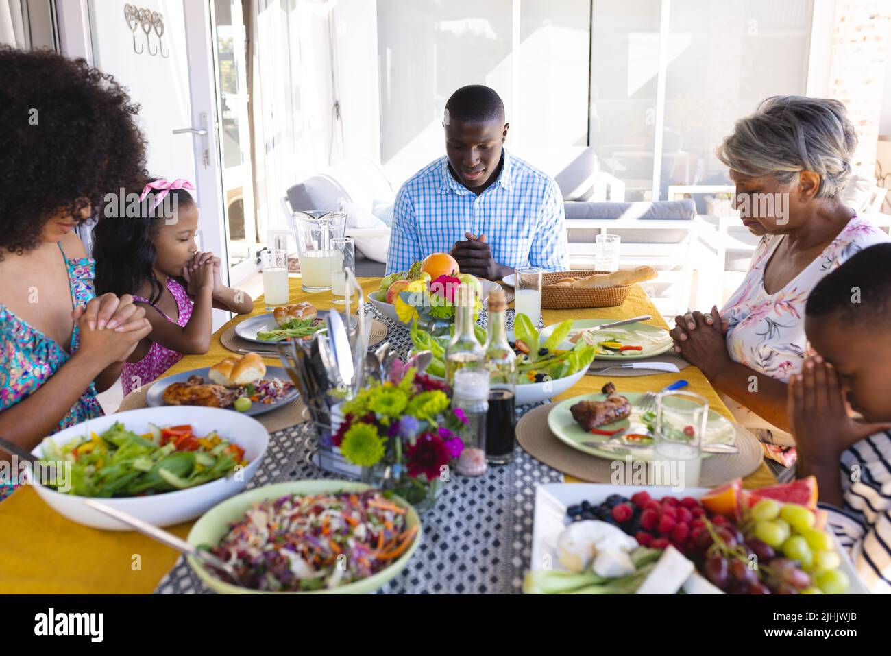 Multiracial multigeneration family with meal on table praying before ...