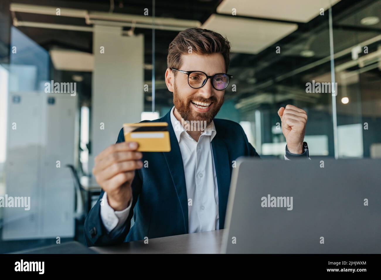 Happy businessman holding credit card in front of laptop and making YES ...