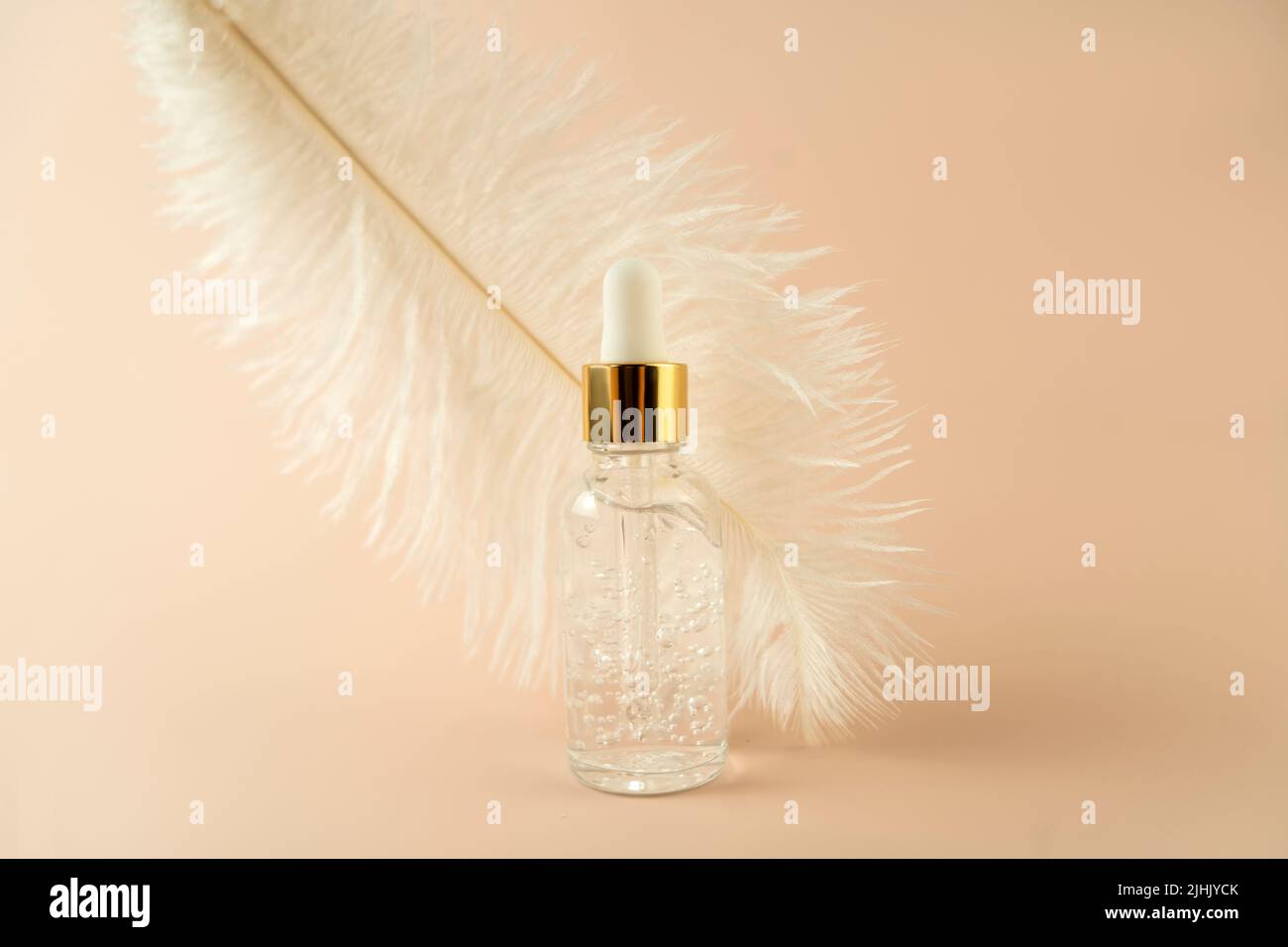 A white feather and a face serum or natural oil standing on a beige ...